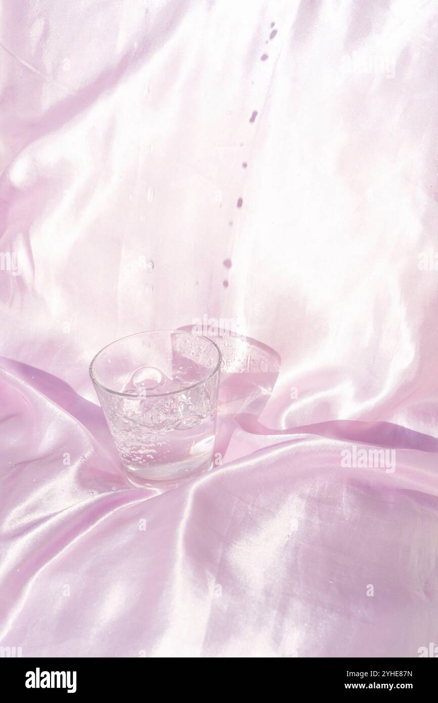 Refreshing Glass of Water on Blush Pink Silk Fabric with water drops ...