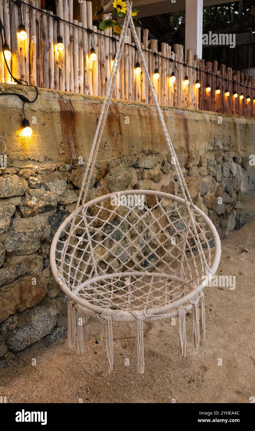 A macrame-style hanging rocking chair with tassels suspended from ropes ...