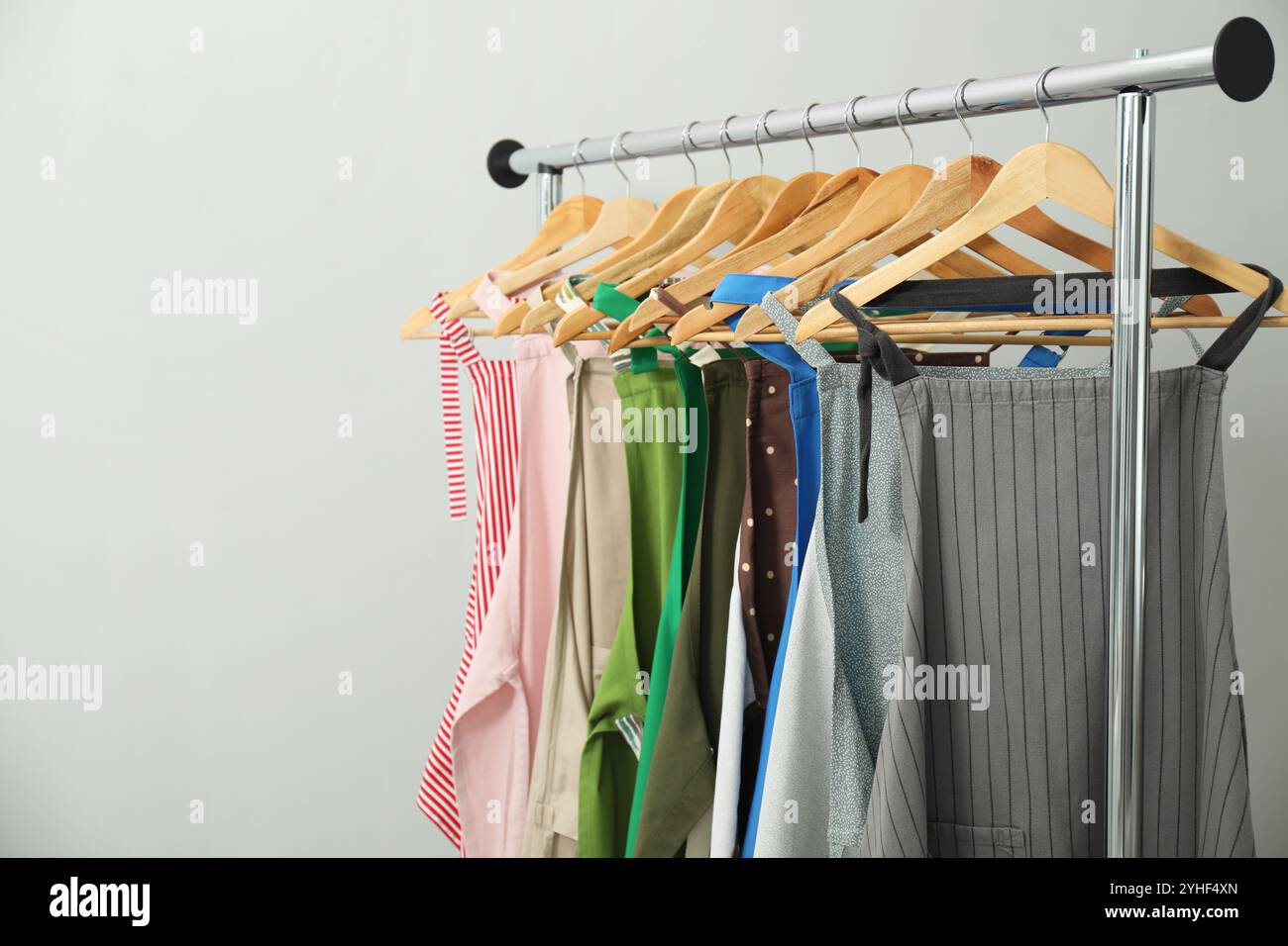 Many chef's aprons on clothing rack near light grey wall, space for ...