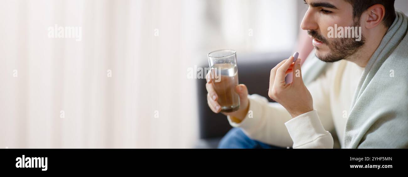 Man taking medication with water while sitting on a couch at home Stock ...
