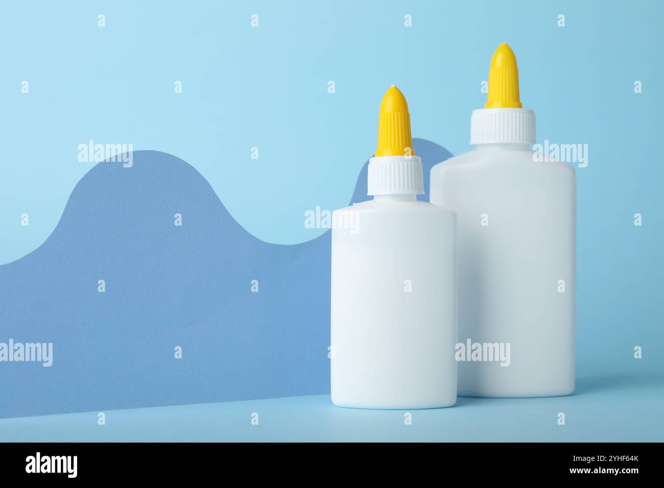 Bottles of glue and paper cutout on light blue background Stock Photo ...