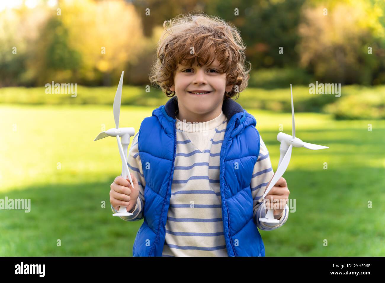 Child boy standing in sunny meadow holding model wind turbine learning ...