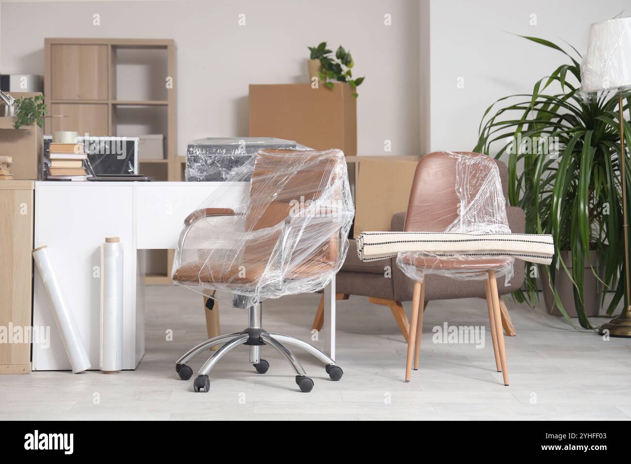 Interior of office with desk, boxes and wrapped chairs in stretch film ...