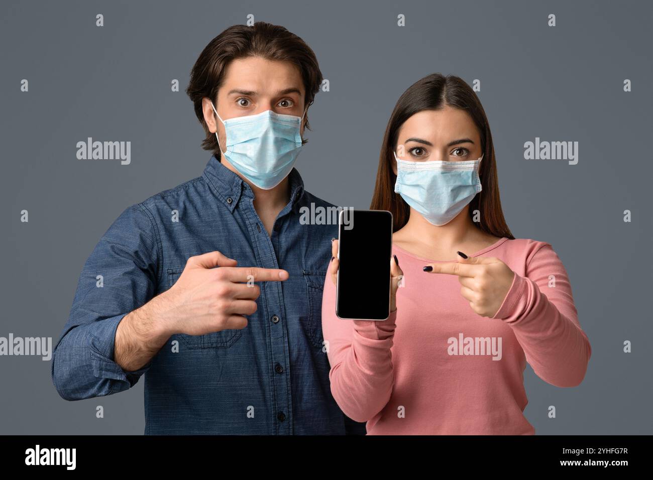 Shocked Couple In Medical Masks Pointing At Smartphone With Black ...
