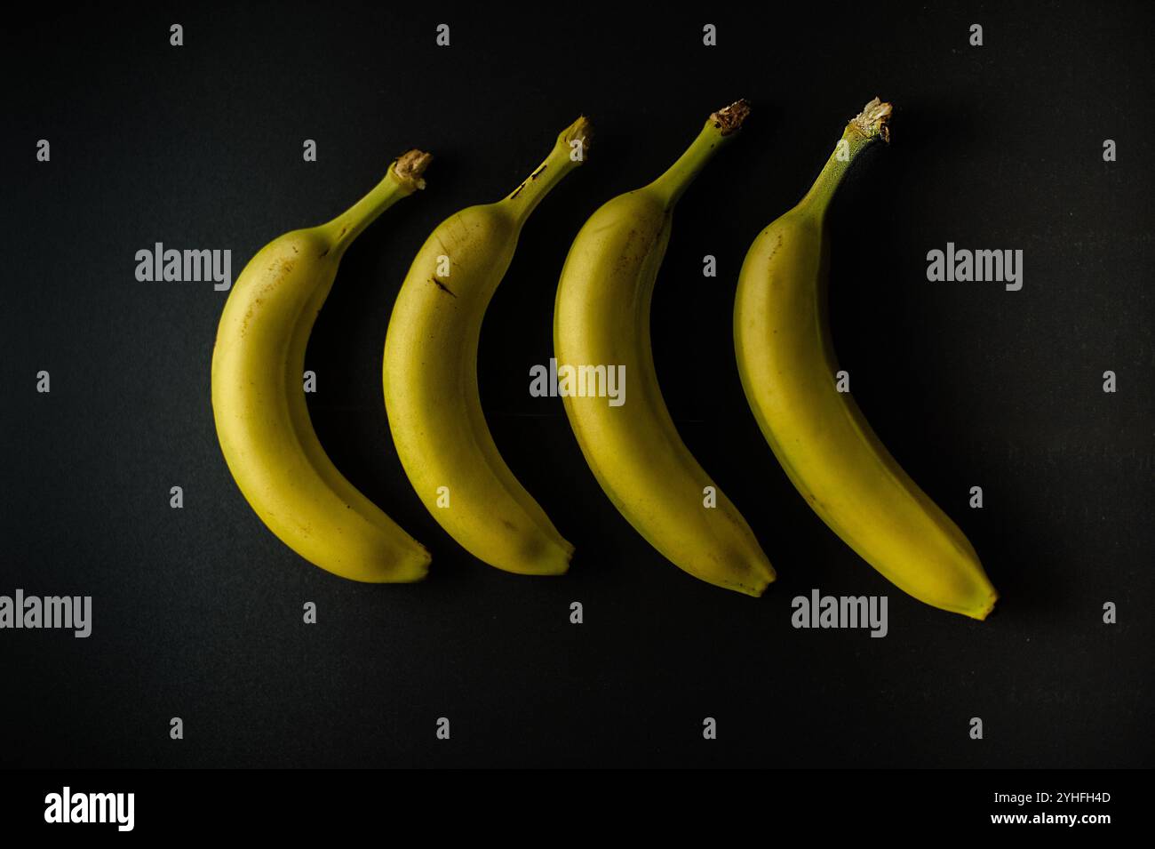 Four bananas are lined up on a black background. The bananas are all ...