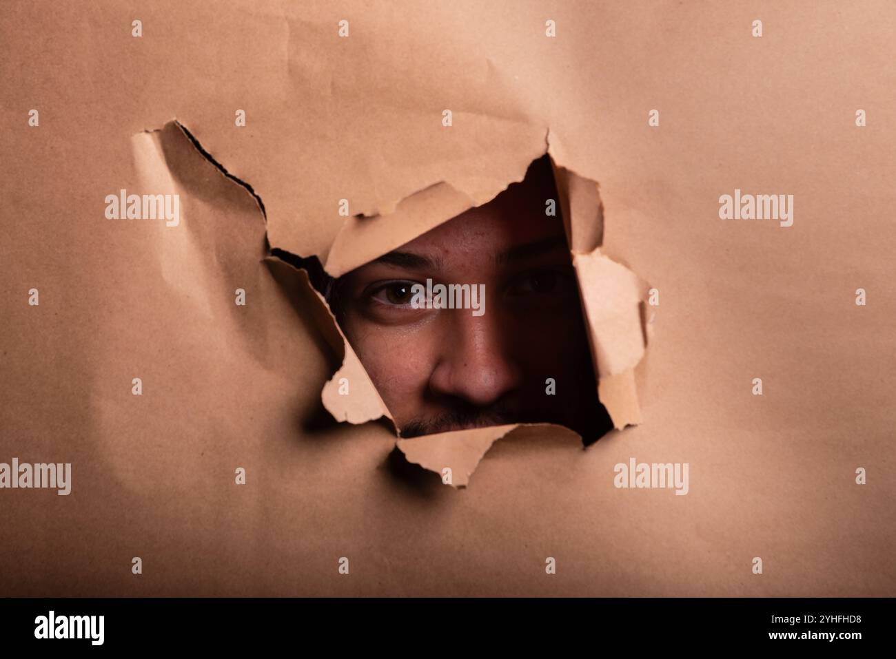 Man looking through a paper hole with his hands pushing the paper aside ...