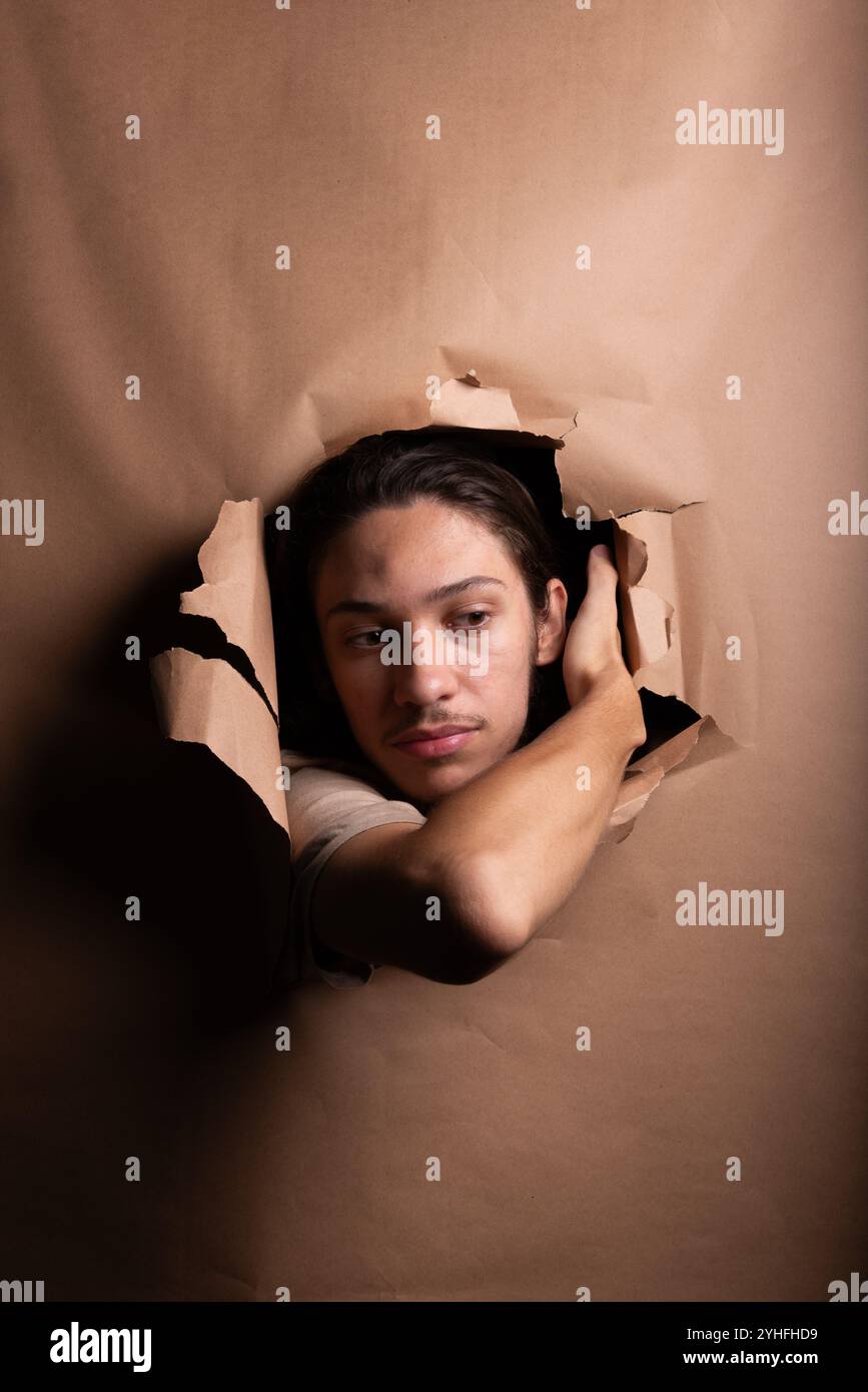 Man's head sticking out and looking through a paper hole with his hands ...