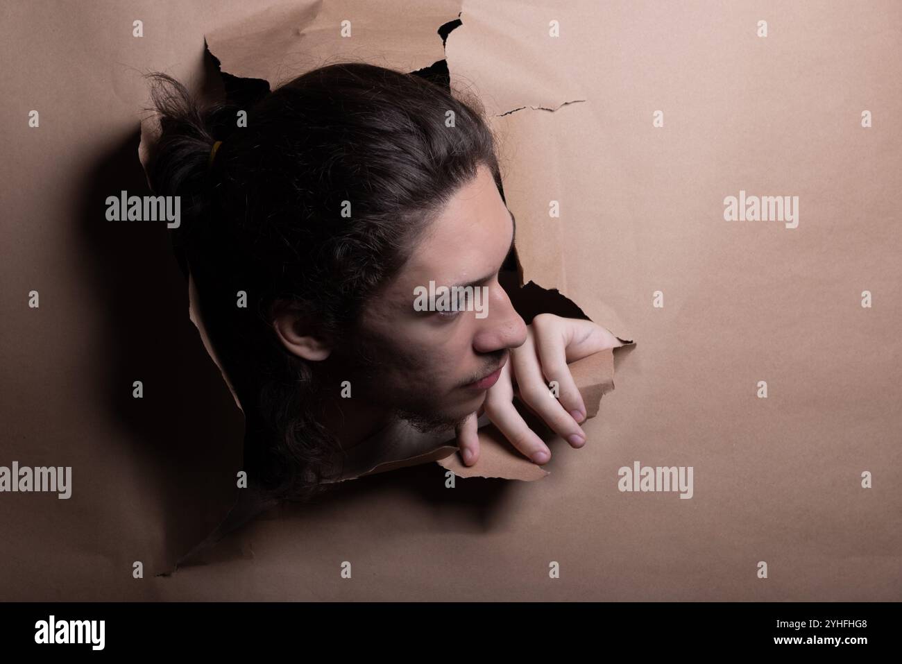 Man face and head sticking out and looking through a hole in brown ...