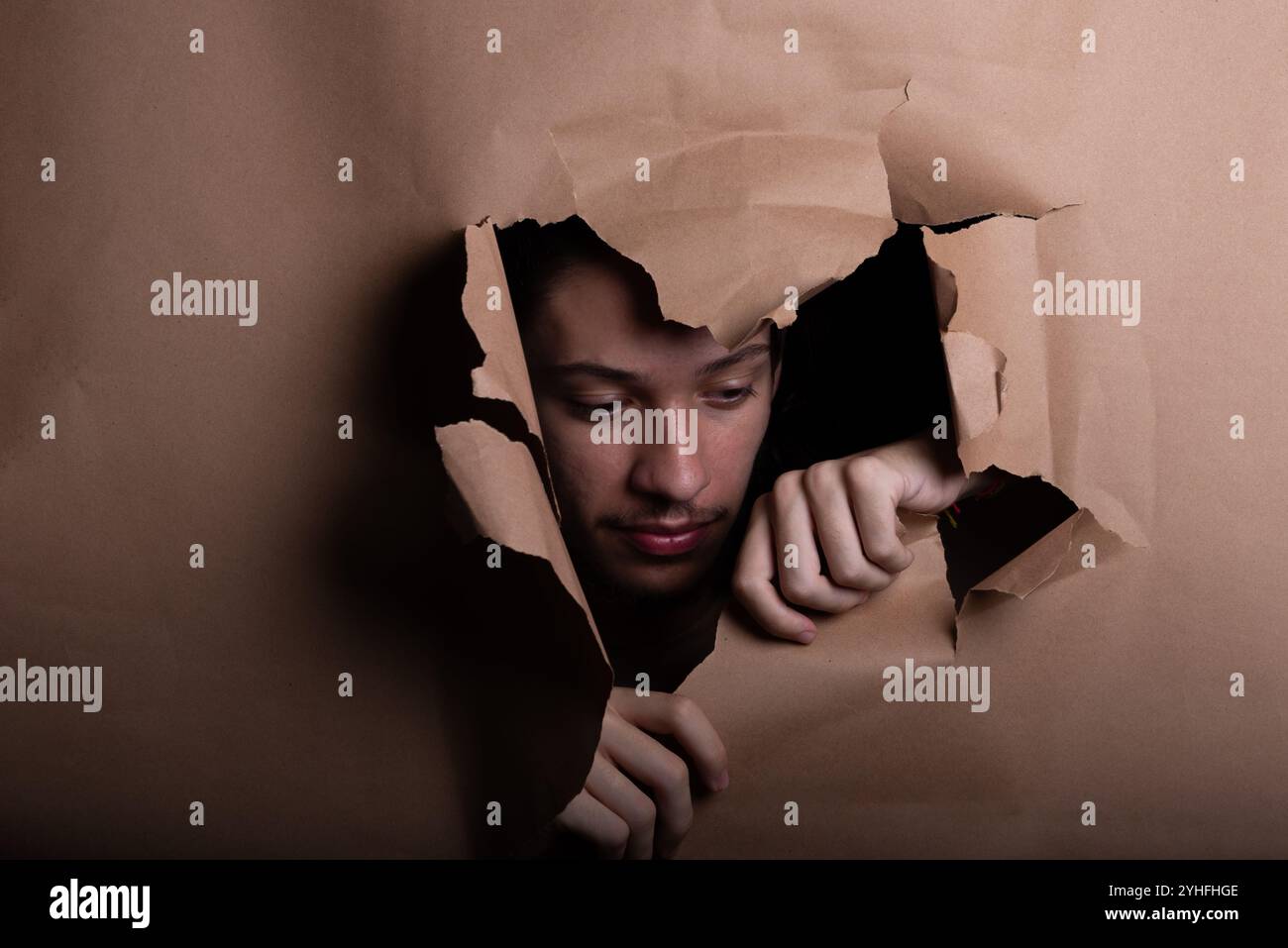 Man's head sticking out and looking through a paper hole with his hands ...