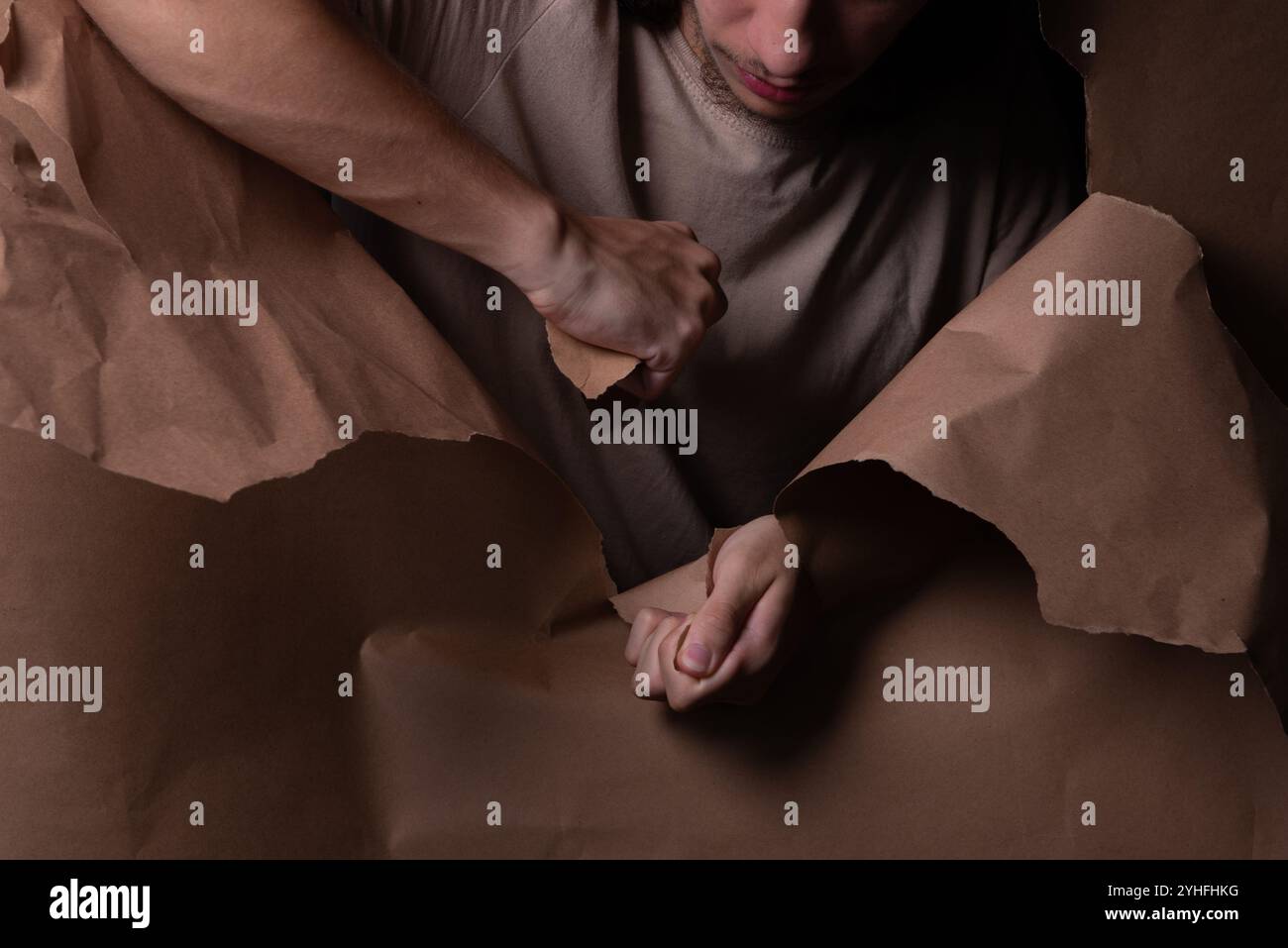 A man peering through a hole in a sheet of brown paper. Tearing the ...