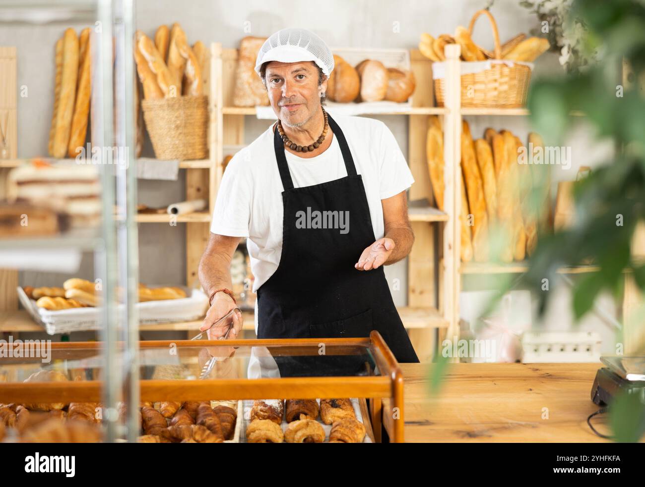 Portrait of friendly baker selling fresh baguettes and croissants in ...
