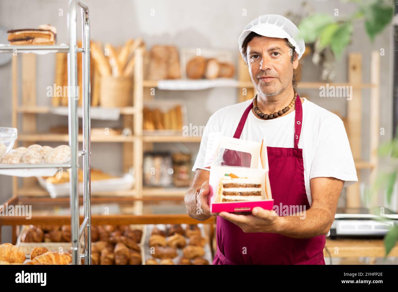 Middle-aged salesman offering a piece of cake packed in box in bakery ...