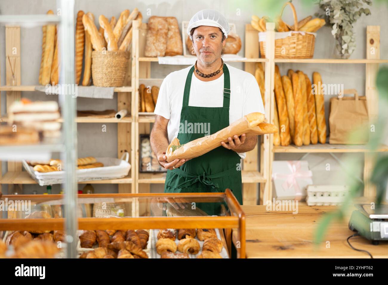 Middle-aged salesman holding paper bag with baguettes in bakery Stock ...