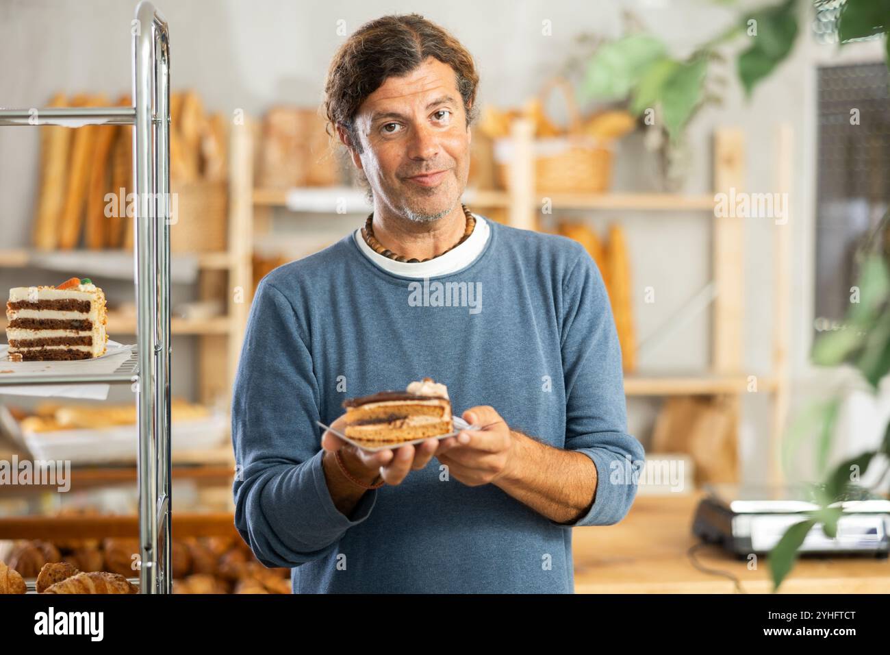 Pleased middle-aged guy holding pastry on paper plate in bakery Stock ...