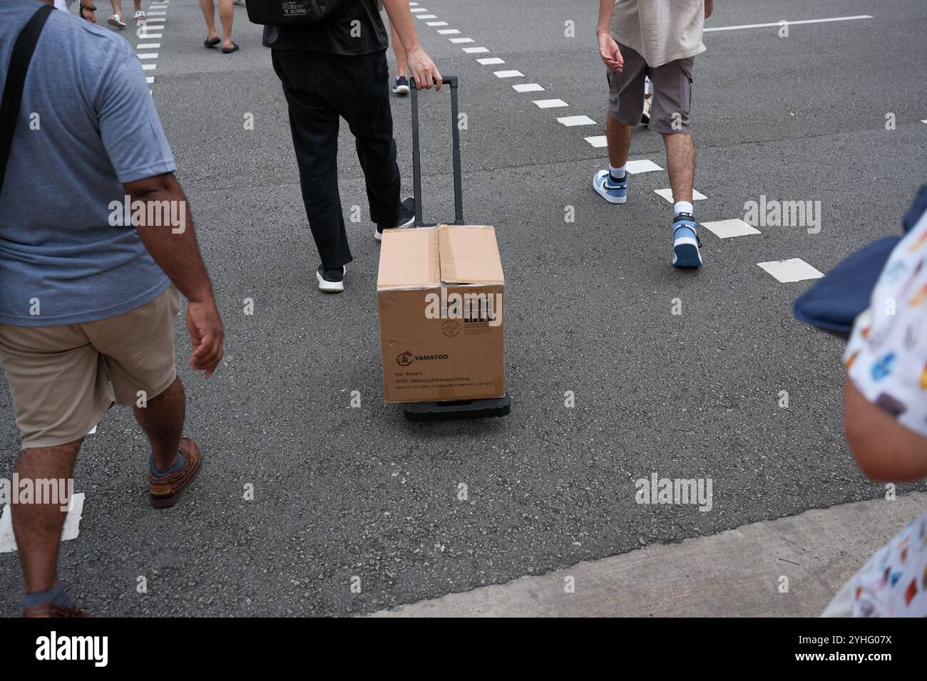 A man pulls a cardboard box on a trolley across a road crossing in ...