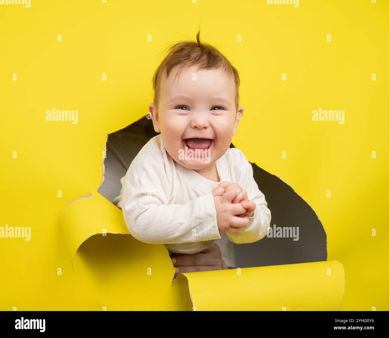 Cheerful baby rips and sticks out through yellow cardboard background ...