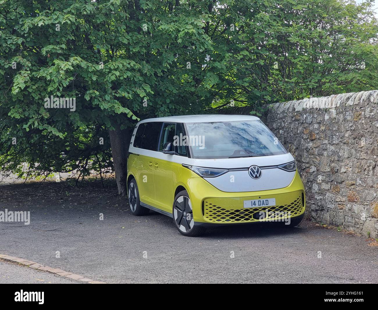 Green & white Volkswagen ID. Buzz, parked under a tree near a stone ...