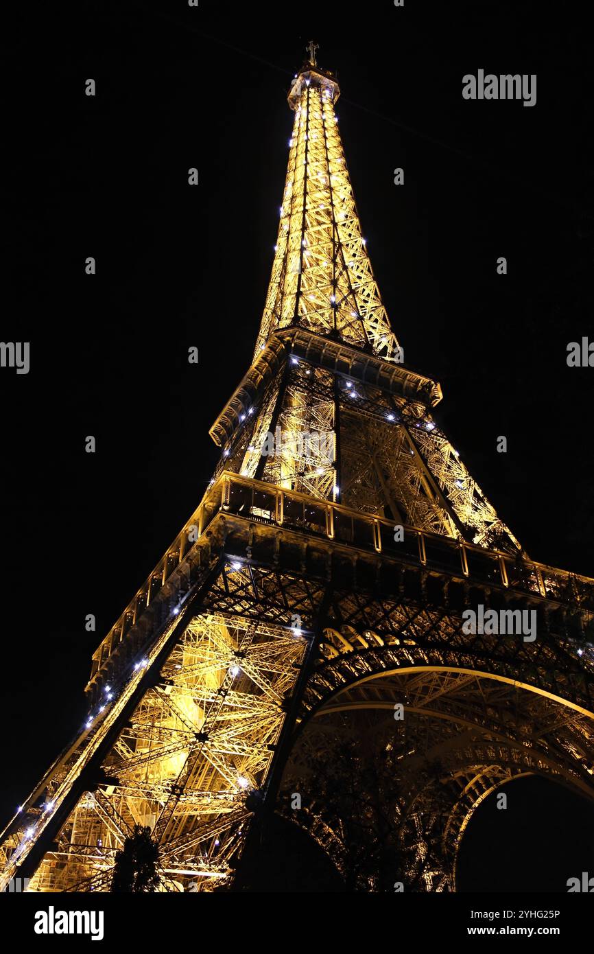 The Eiffel Tower glowing with golden lights against the night sky, showcasing its majestic ...