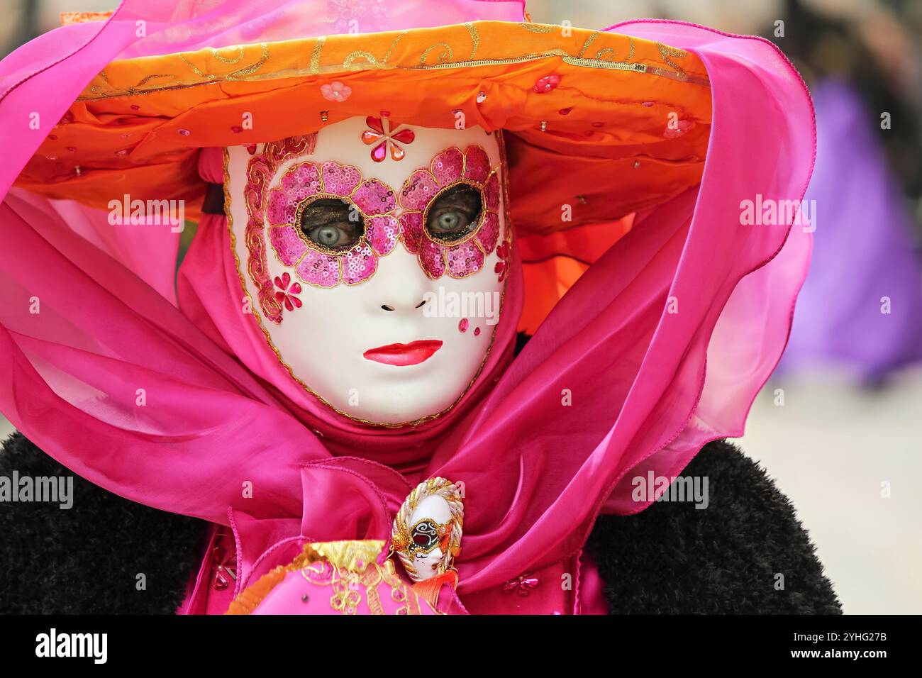 A close-up of a person wearing an elaborate pink Venetian carnival mask ...