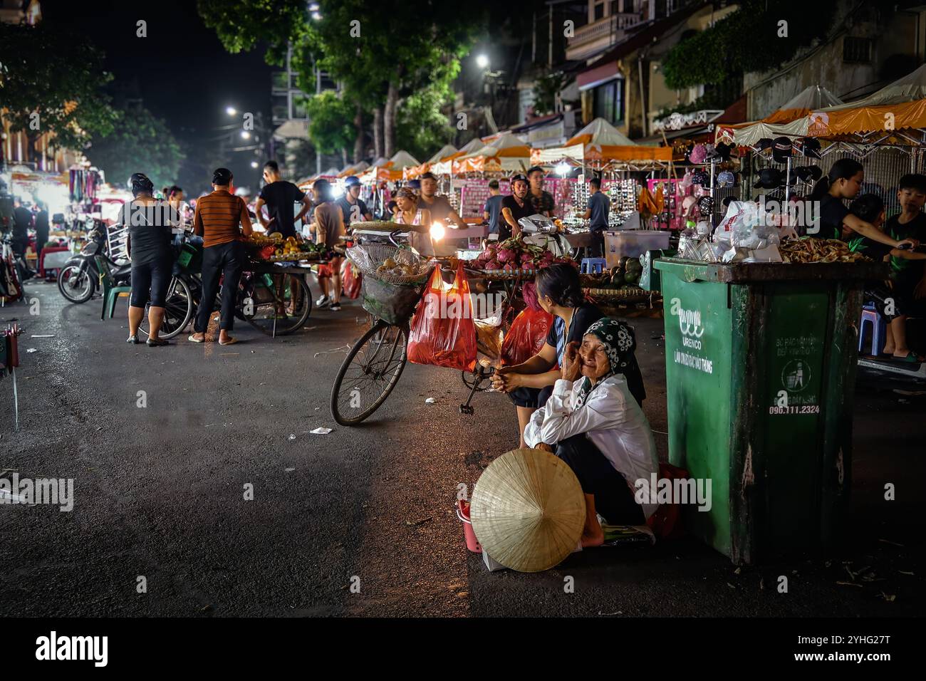 A vibrant night market scene in Hanoi, where locals gather to sell fruits and goods under the ...