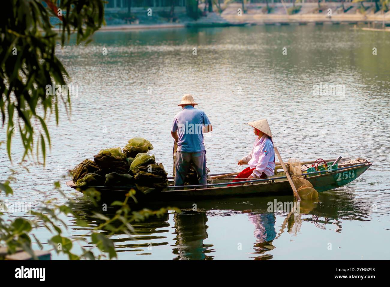A man and woman in traditional hats work on a small boat on a serene ...