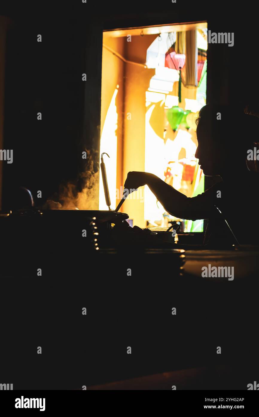 A silhouette of a woman cooking in a dimly lit kitchen, with warm ...