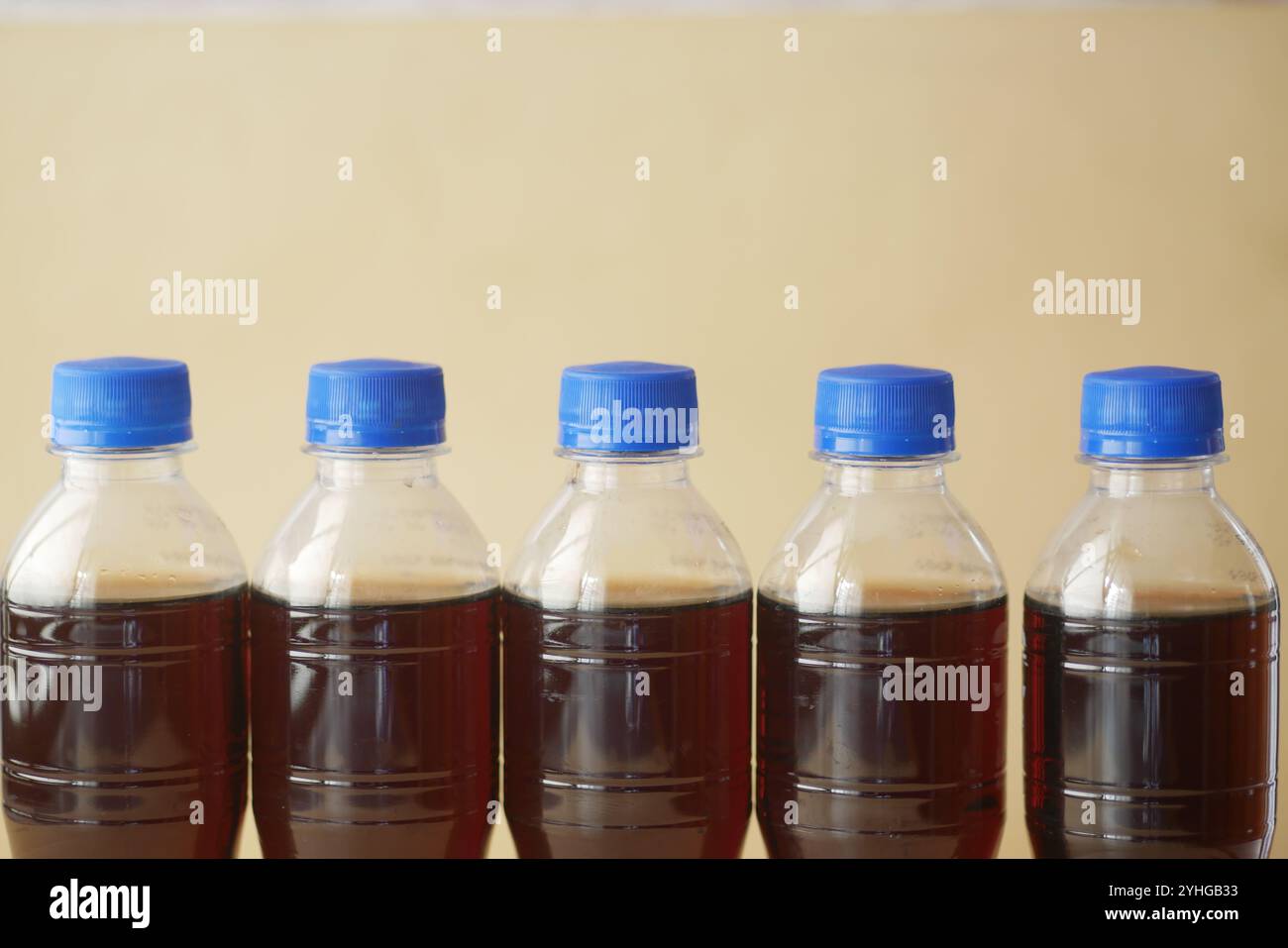 Five bottles with dark liquid and blue lids are displayed on a ...