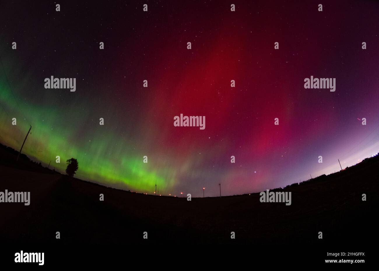 A fisheye perspective captures the sweeping aurora borealis above, with ...