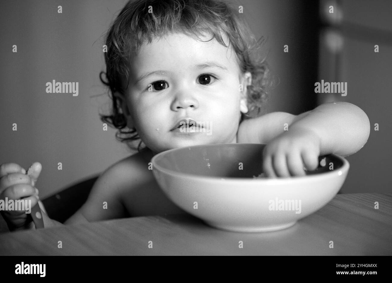 Funny baby eating food himself with a spoon on kitchen. Child nutrition ...