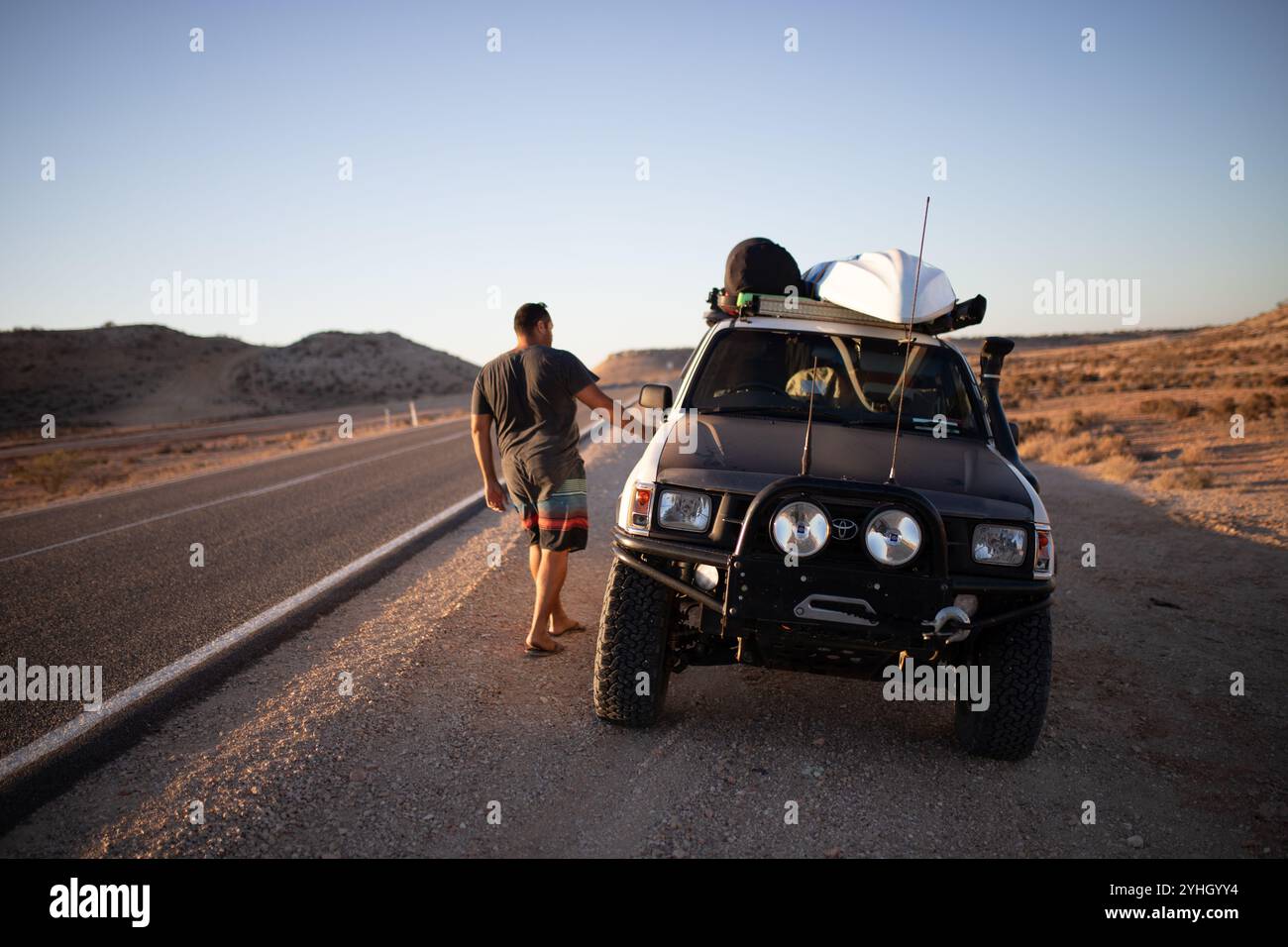 At sunset, a tanned man climbs into his kitted-out 4WD ute parked along ...