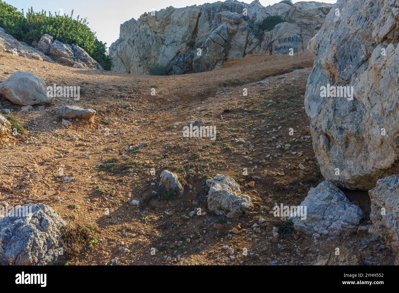 Scenic rocky terrain with sunlit path leading into a lush hillside at ...