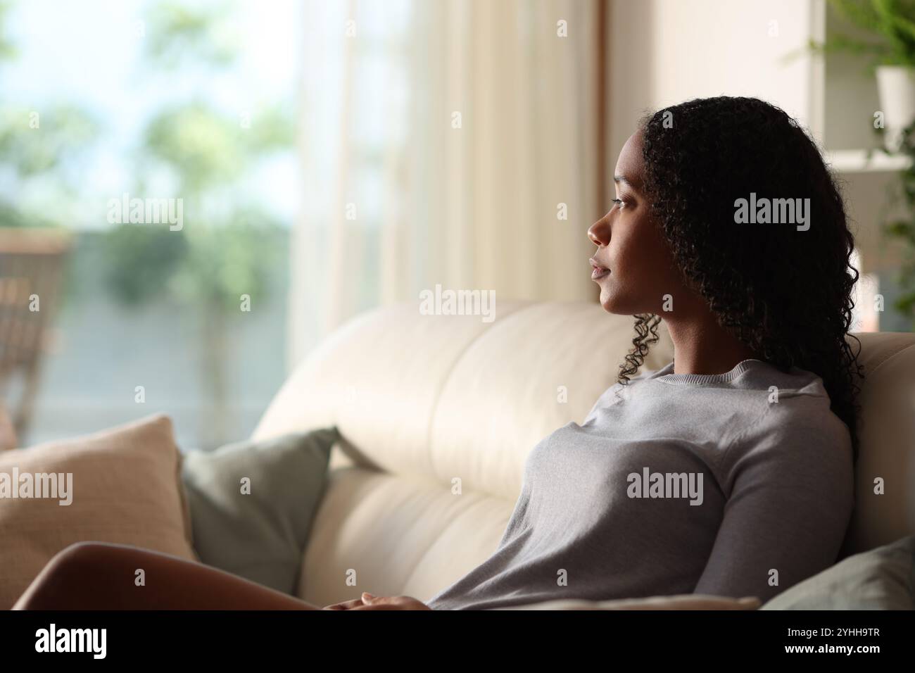 Backlight of a black woman contemplating through a window at home Stock ...