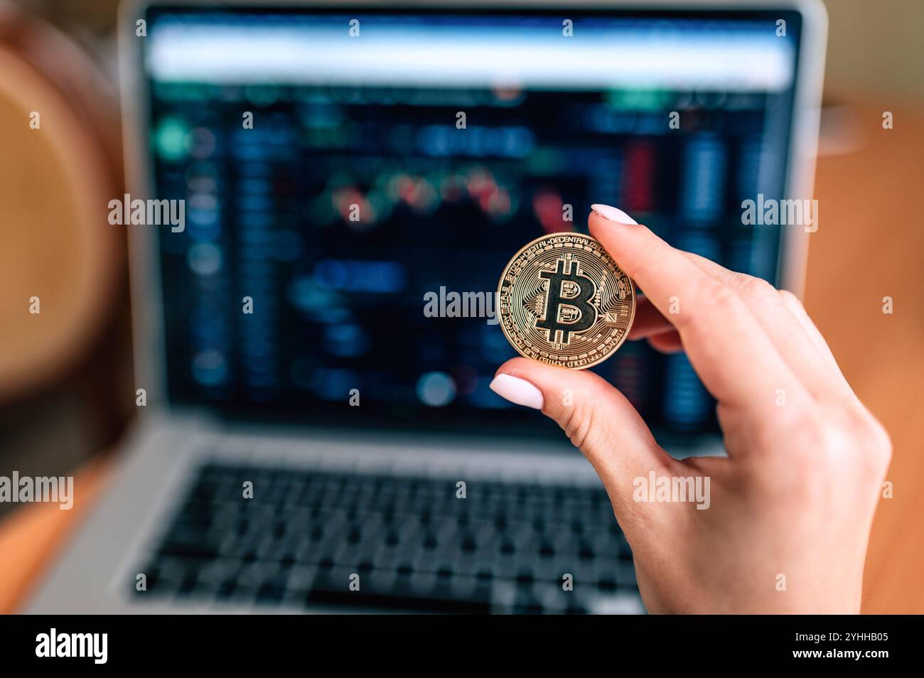 A female hand holding up a gold bitcoin coin token in front of a laptop ...