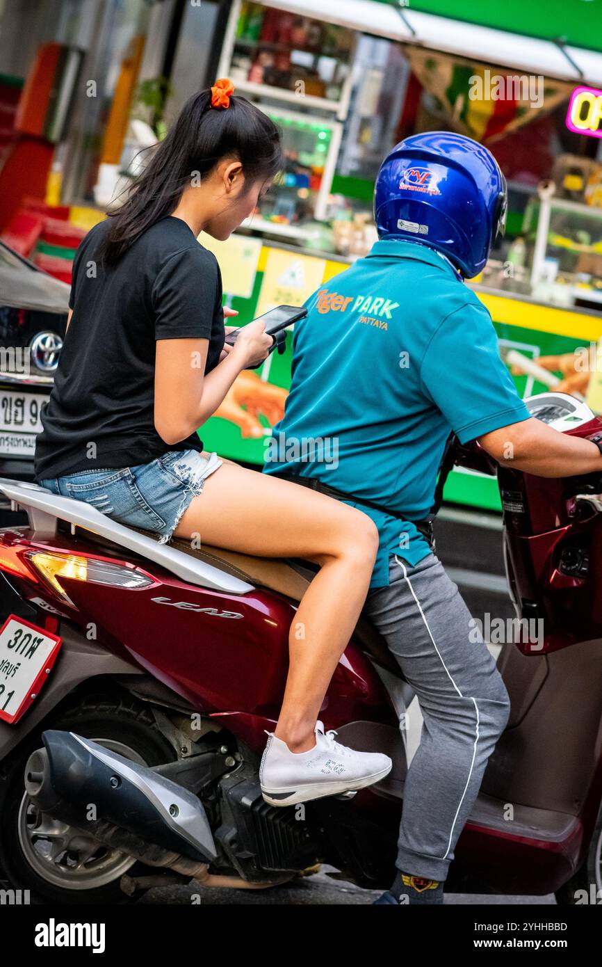 A beautiful young Thai lady rides on the back of a motorbike taxi along ...