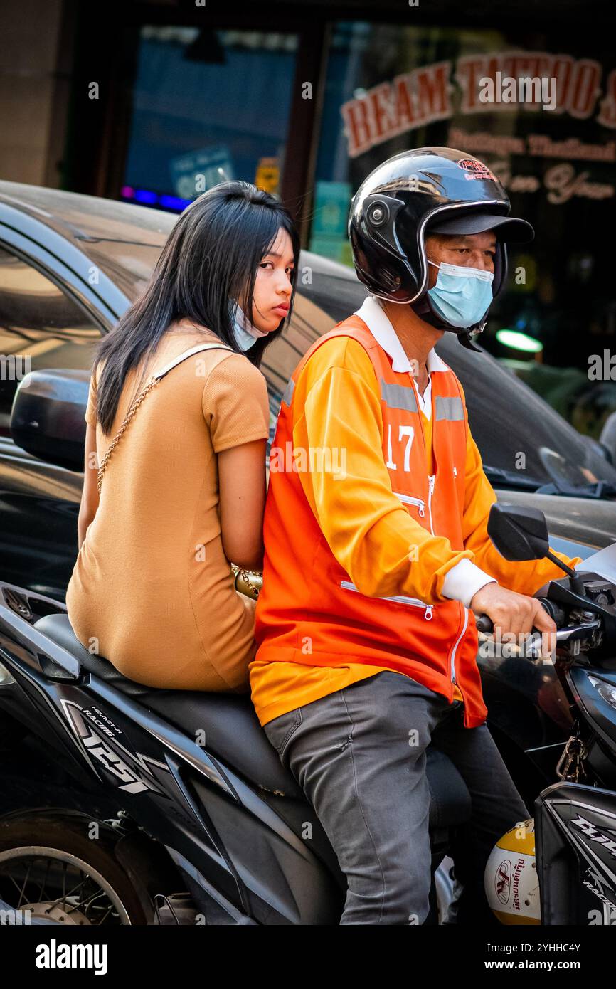 A beautiful young Thai lady rides on the back of a motorbike taxi along ...