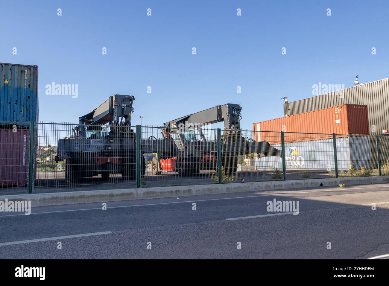 Two reach stackers are parked behind a fence in a container terminal ...