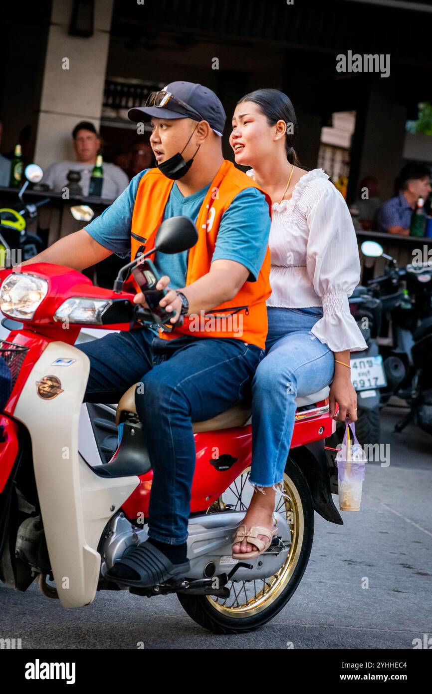 A beautiful young Thai lady rides on the back of a motorbike taxi along ...