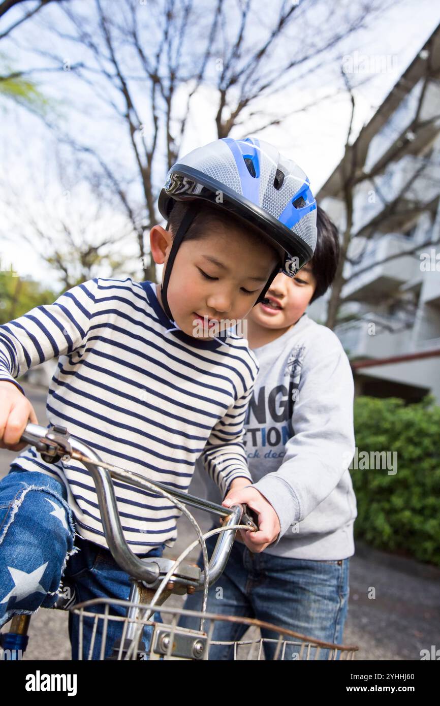 Girl giving a boy practice riding a bicycle Stock Photo - Alamy