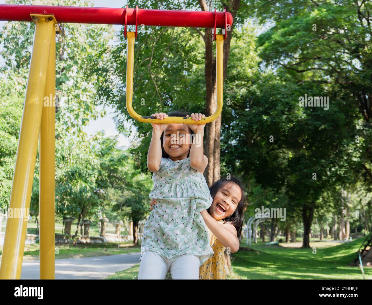 Cute sisters having fun hanging on monkey bars in an outdoor park. Children playing in the ...
