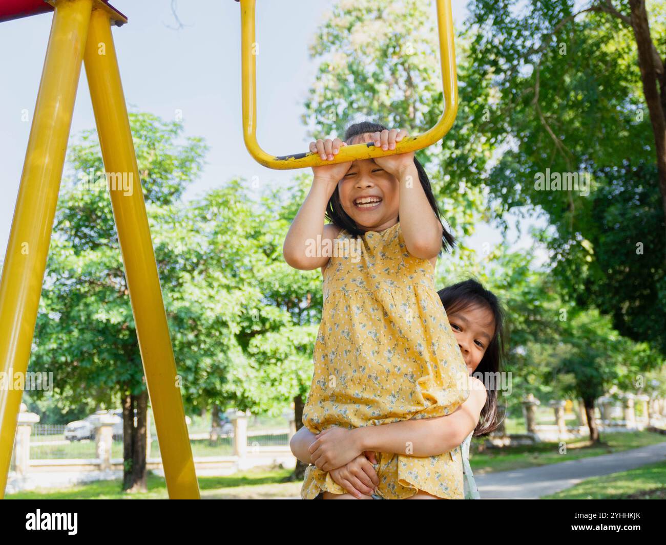 Cute sisters having fun hanging on monkey bars in an outdoor park. Children playing in the ...
