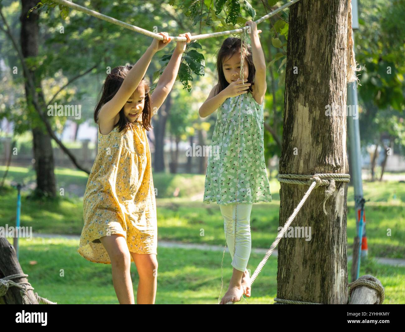 Cute sisters are having fun hanging from ropes in an outdoor park ...