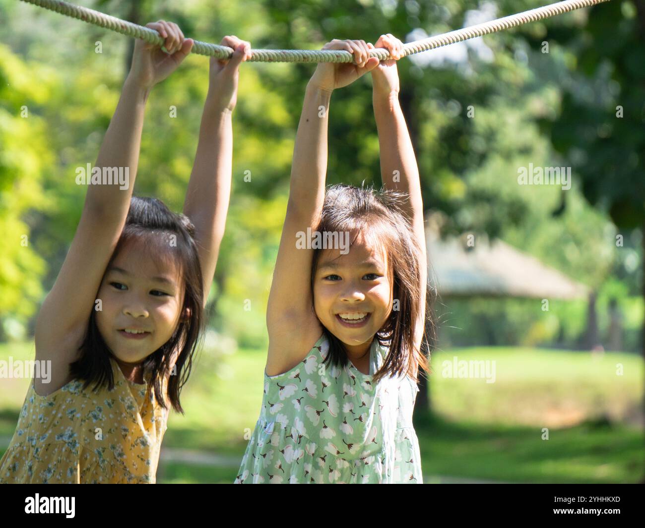 Cute sisters are having fun hanging from ropes in an outdoor park ...