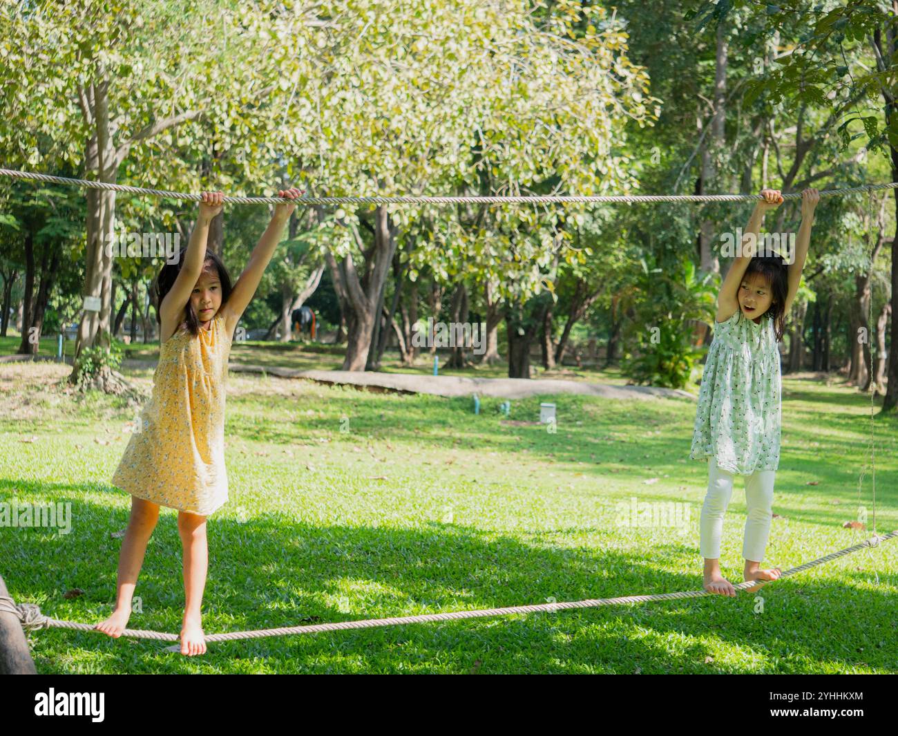 Cute sisters are having fun hanging from ropes in an outdoor park ...