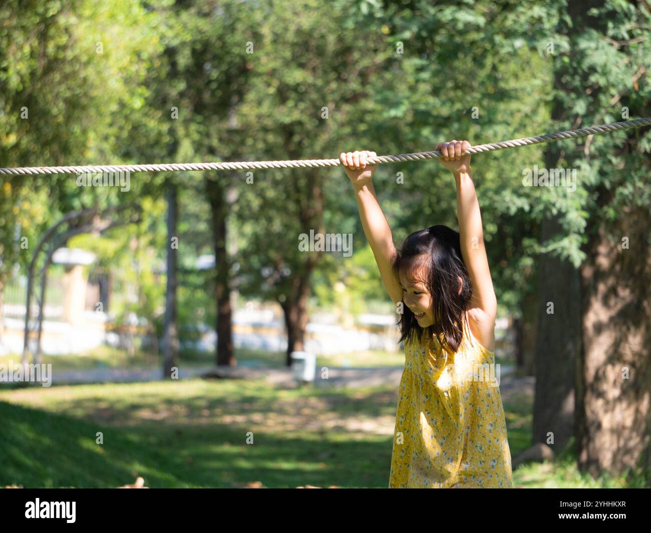 Cute sisters are having fun hanging from ropes in an outdoor park ...
