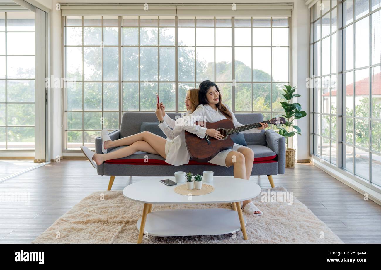 Two friend sit on sofa in a bright living room with large glass wall ...