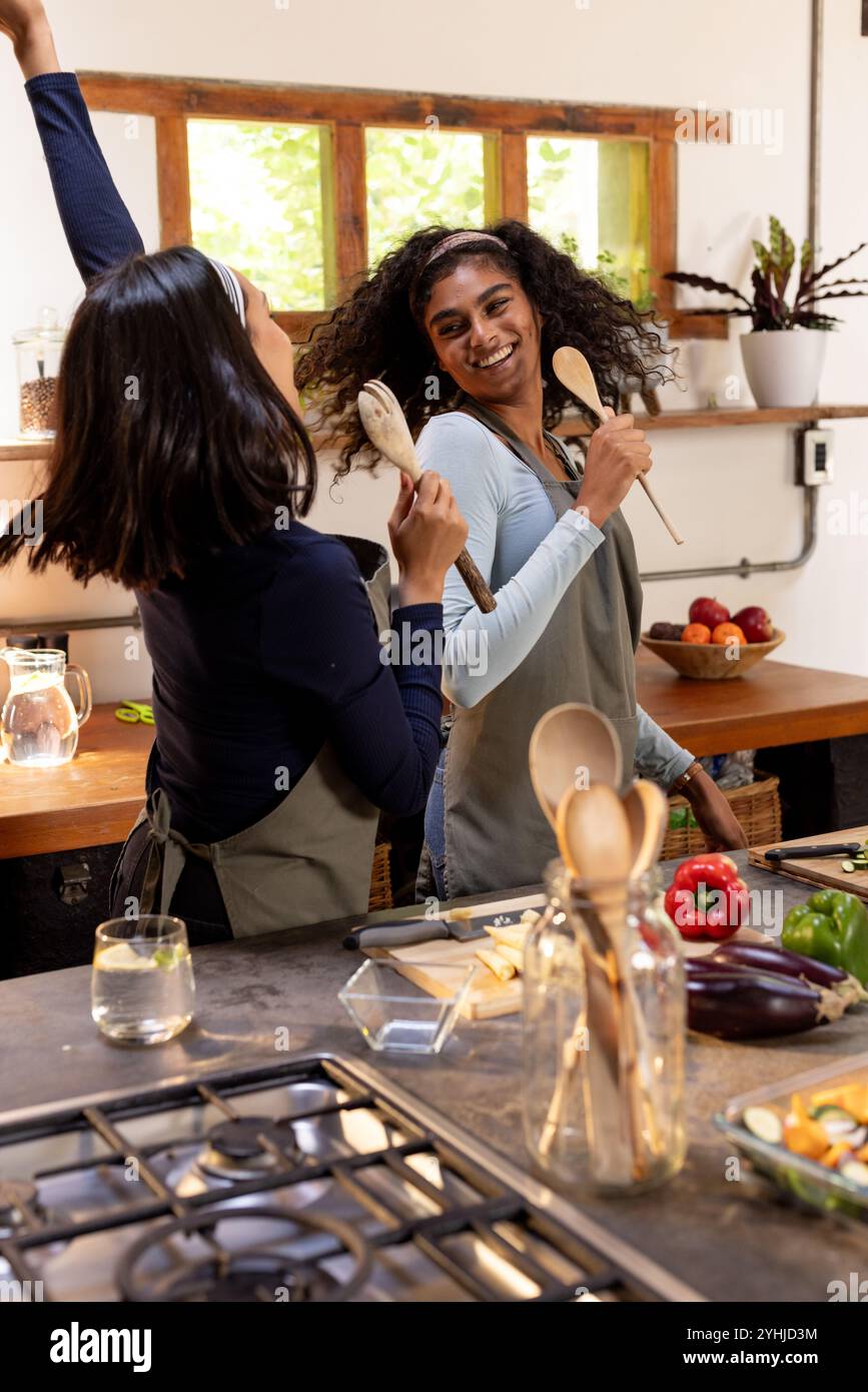 Two multiracial female friends joyfully cooking together in kitchen ...