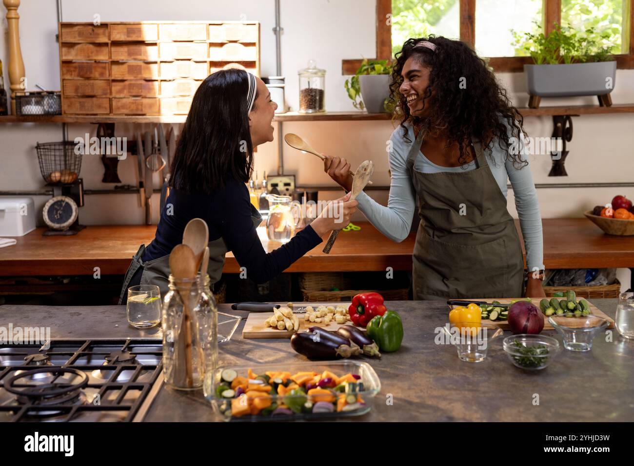 Two multiracial female friends cooking together in kitchen, laughing ...