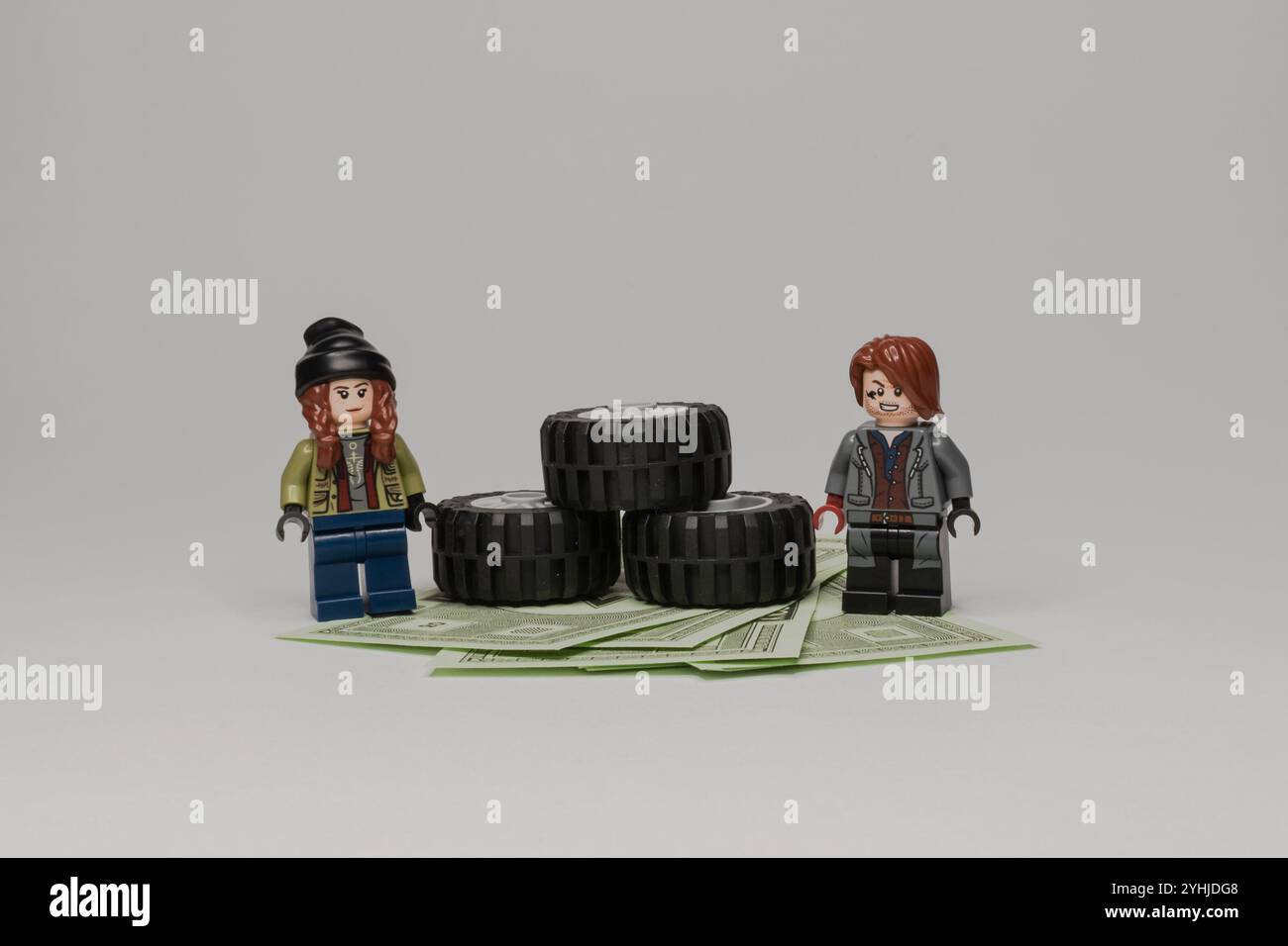 Lego couple standing next to a pile of tyres and money underneath them ...