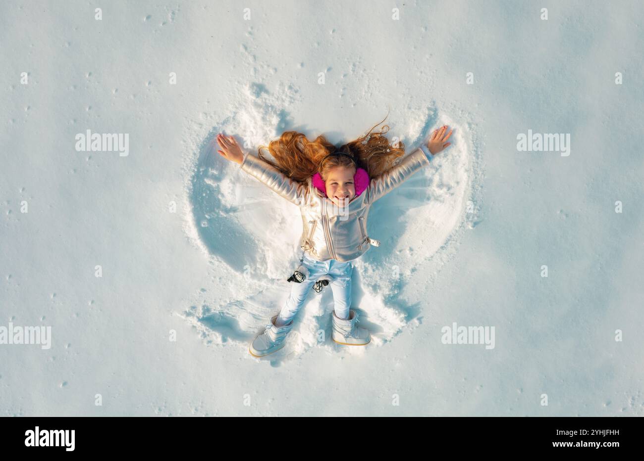 Snow angel made by a kid in the snow. Smiling child lying on snow with ...