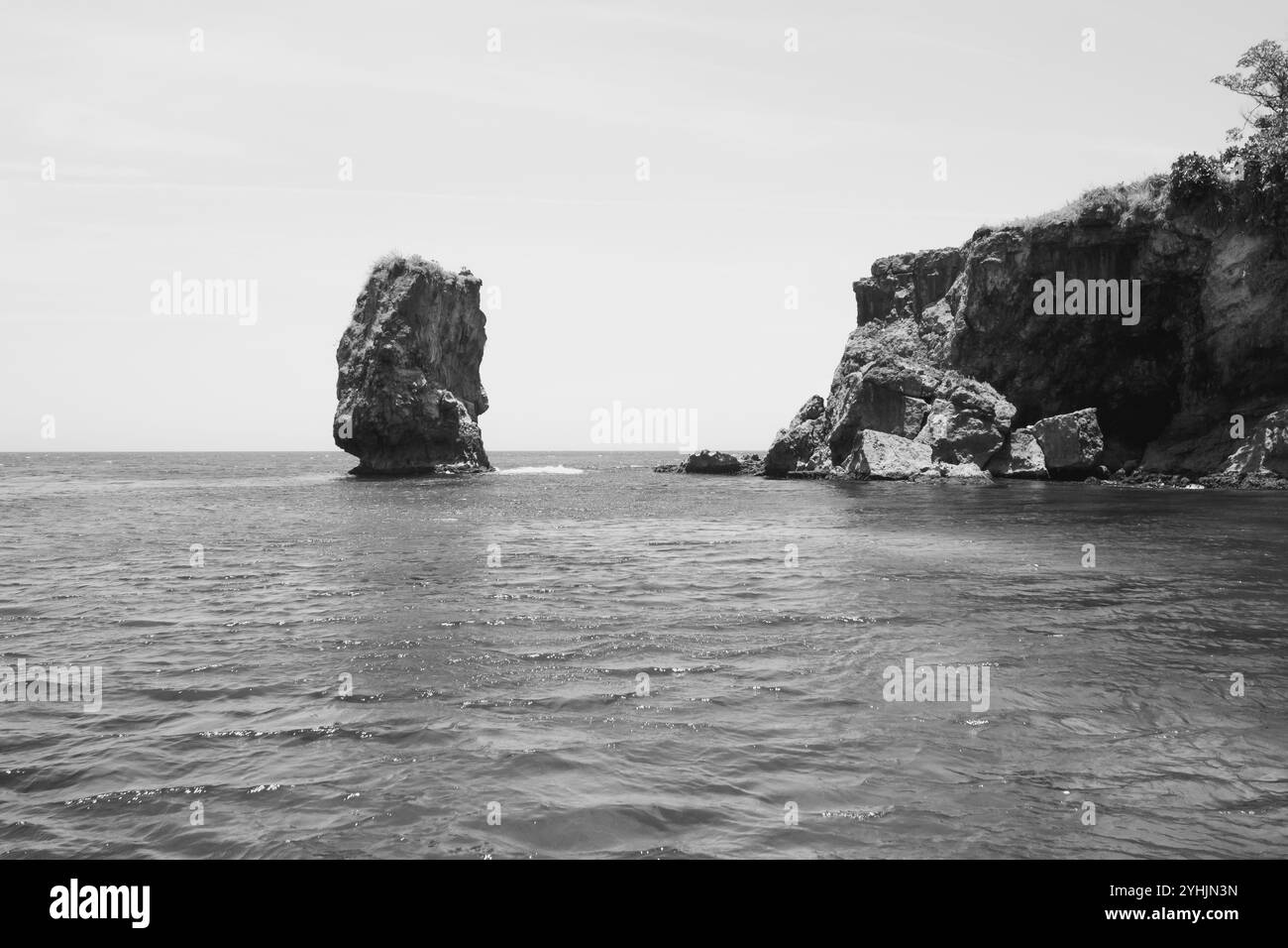 Gentle waves lap against rugged cliffs and a towering rock formation ...